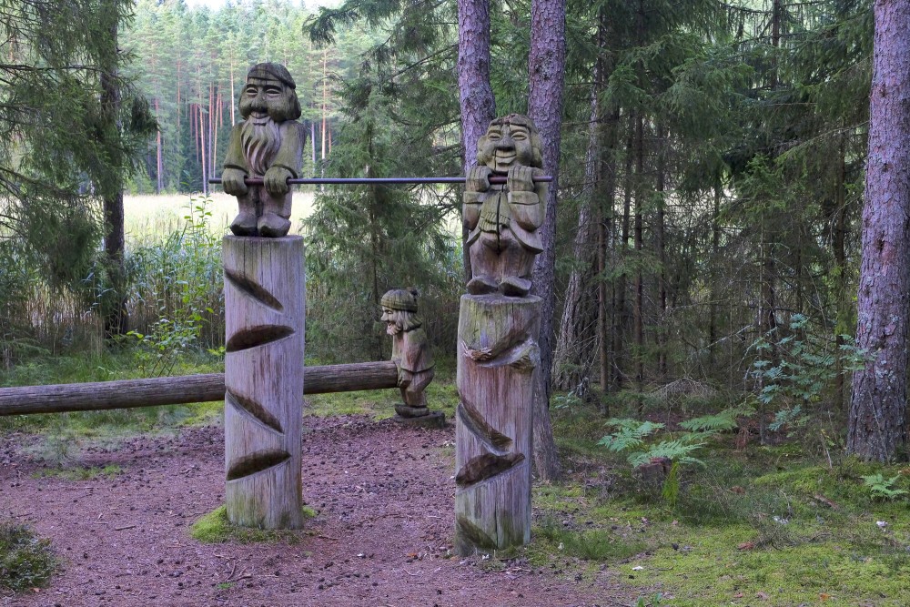 Wooden sculptures by a forest obstacle with a log between posts - redzet.lv