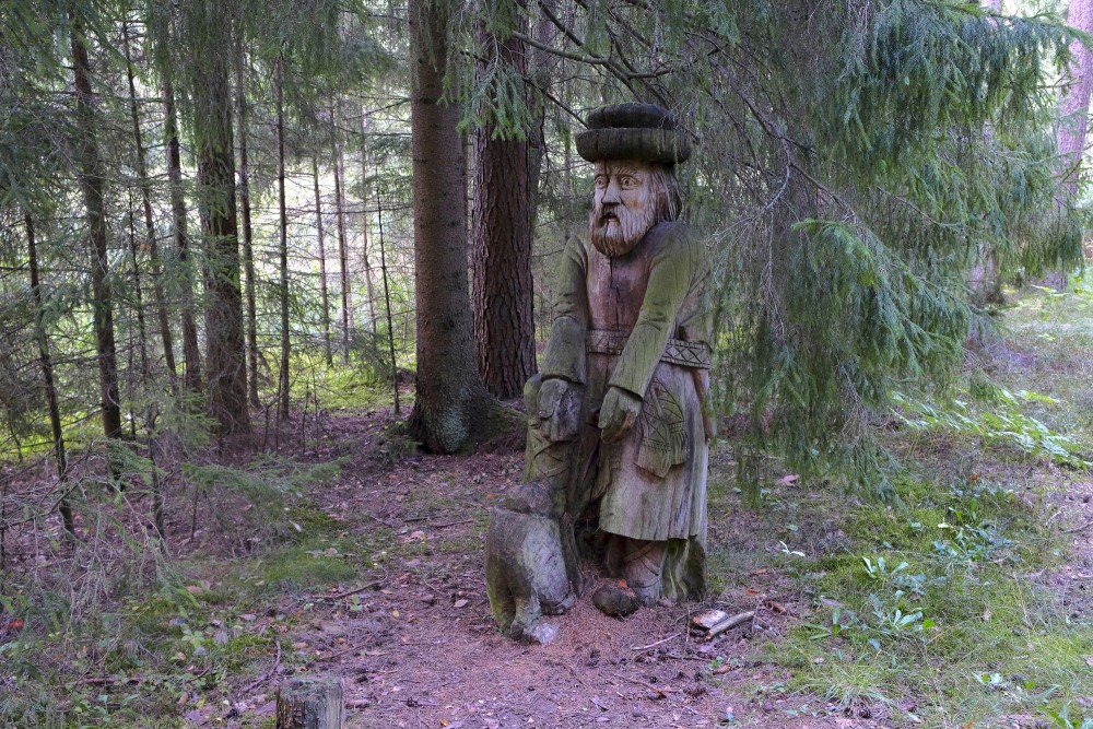Wooden female sculpture in the forest by a trail with a log bench ...