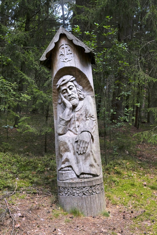 Wooden female sculpture in the forest by a trail with a log bench ...