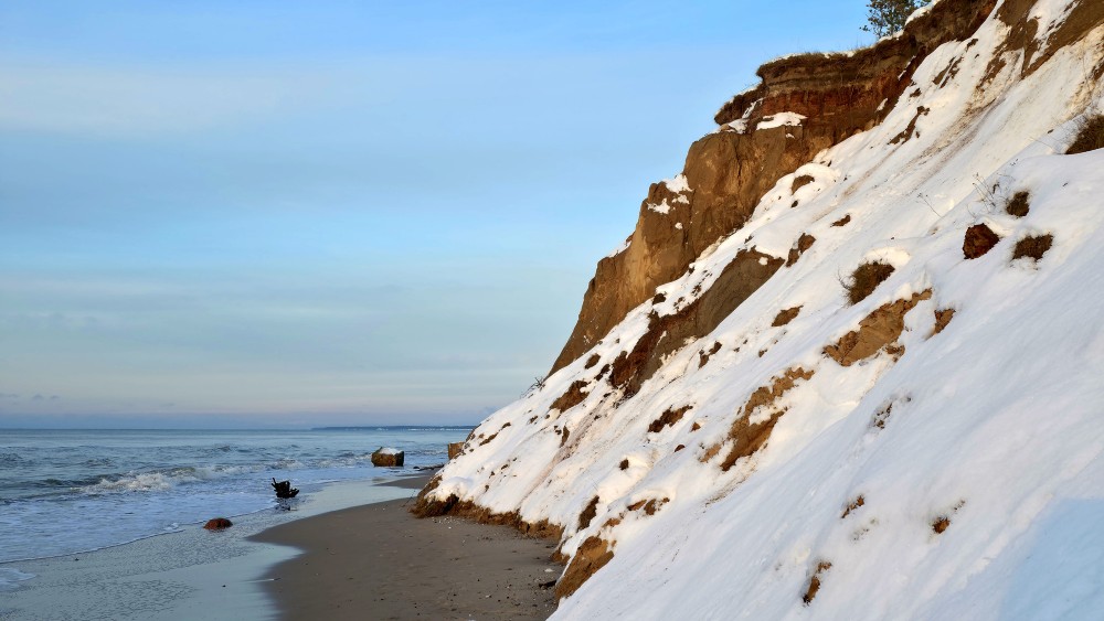 Snowy Jurkalne steep bank by the sea with sandy beach and calm horizon ...