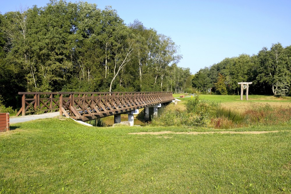 Pedestrian bridge over the Bārta River with aquatic plants and park ...