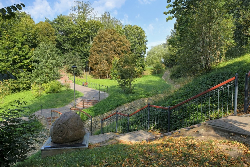 Winding paved path under tall trees in Salantai City Park - redzet.lv